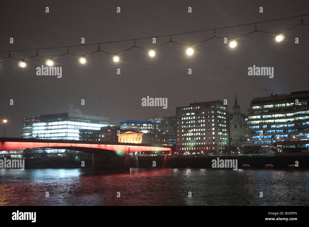 Snow falls at night in London by the river Thames on a cold snowy ...