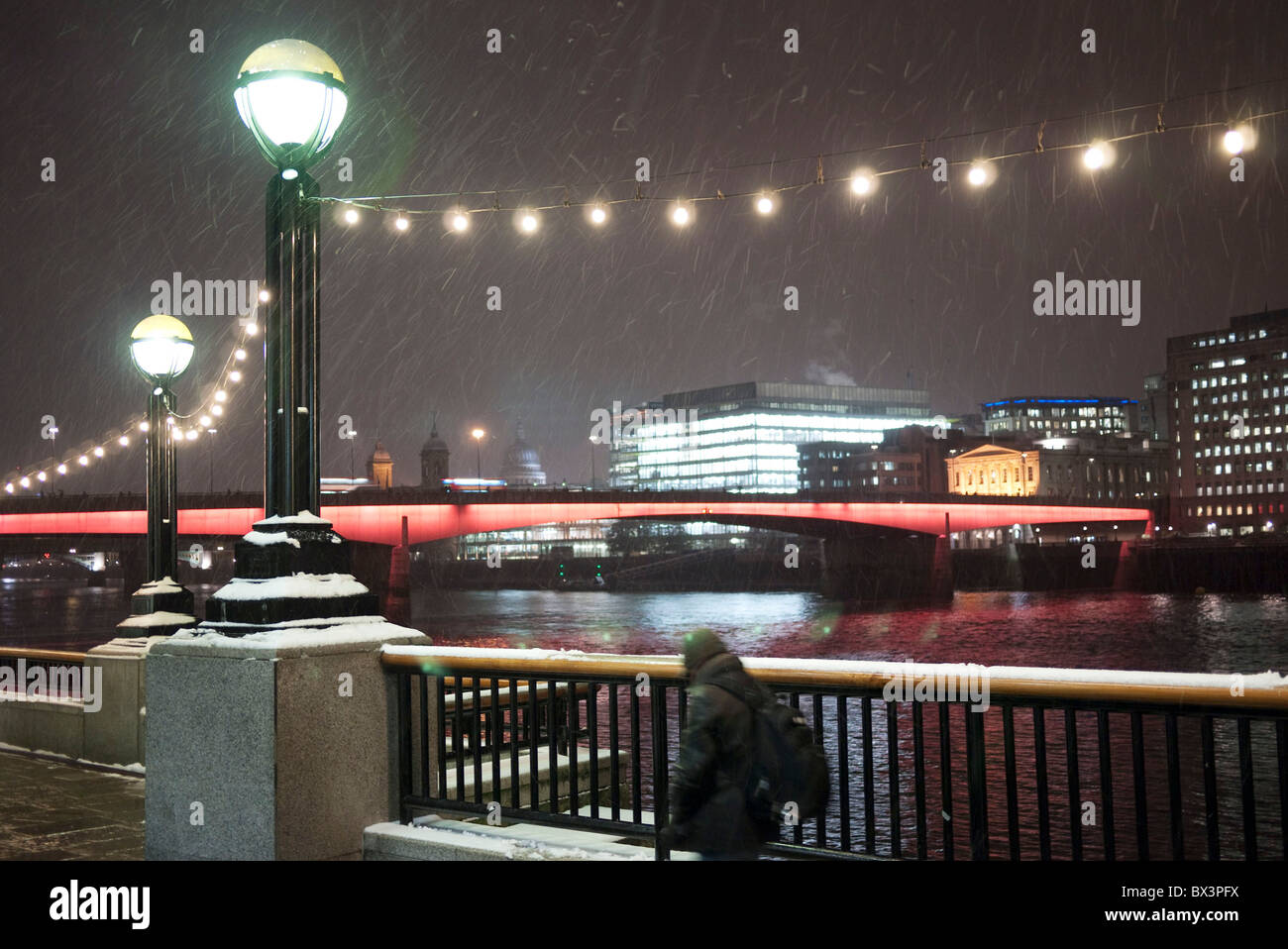 Snow falls at night in London by the river Thames on a cold snowy ...