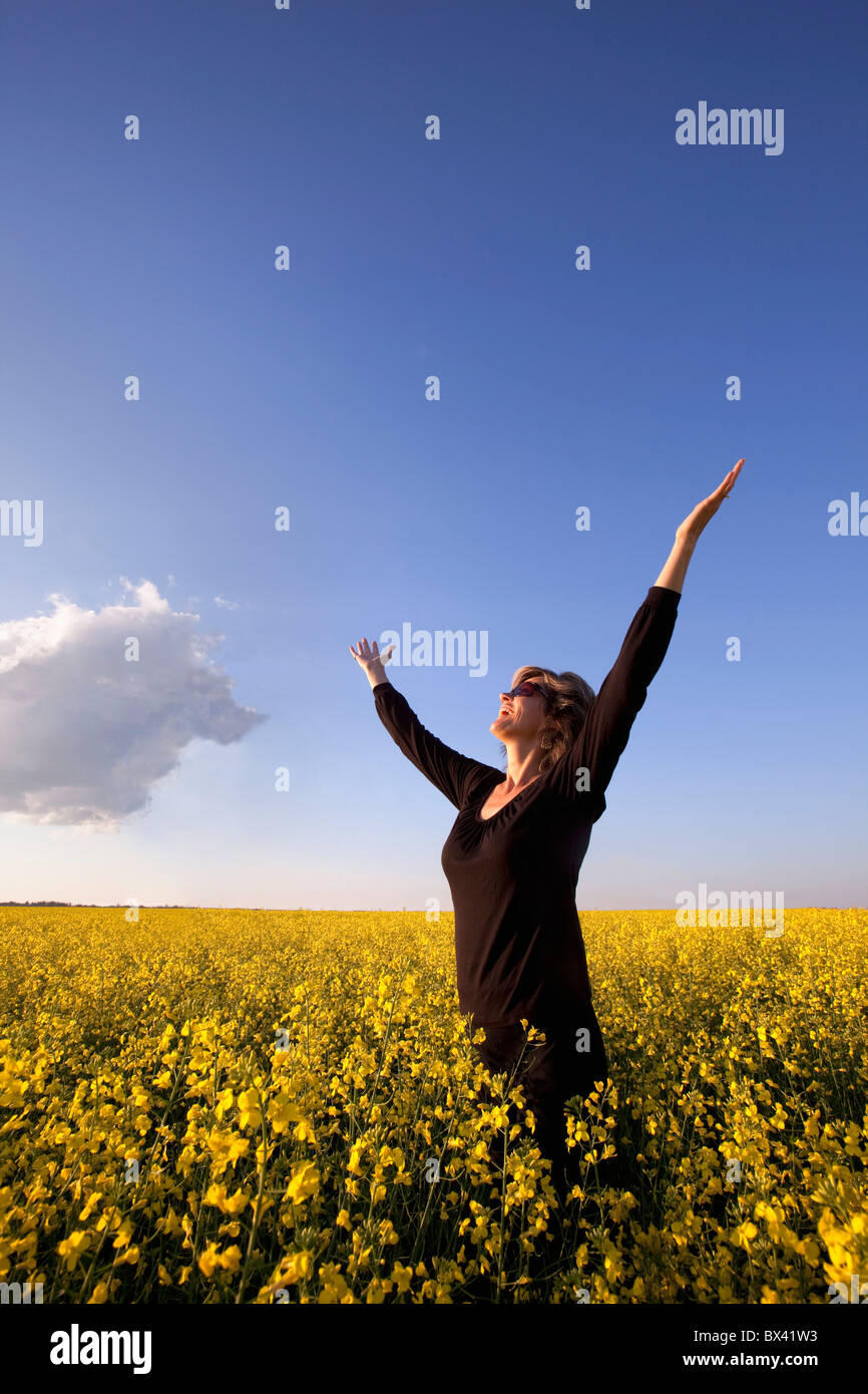 Woman Taking In The Sun With Her Arms Raised In A Canola Field; Alberta ...