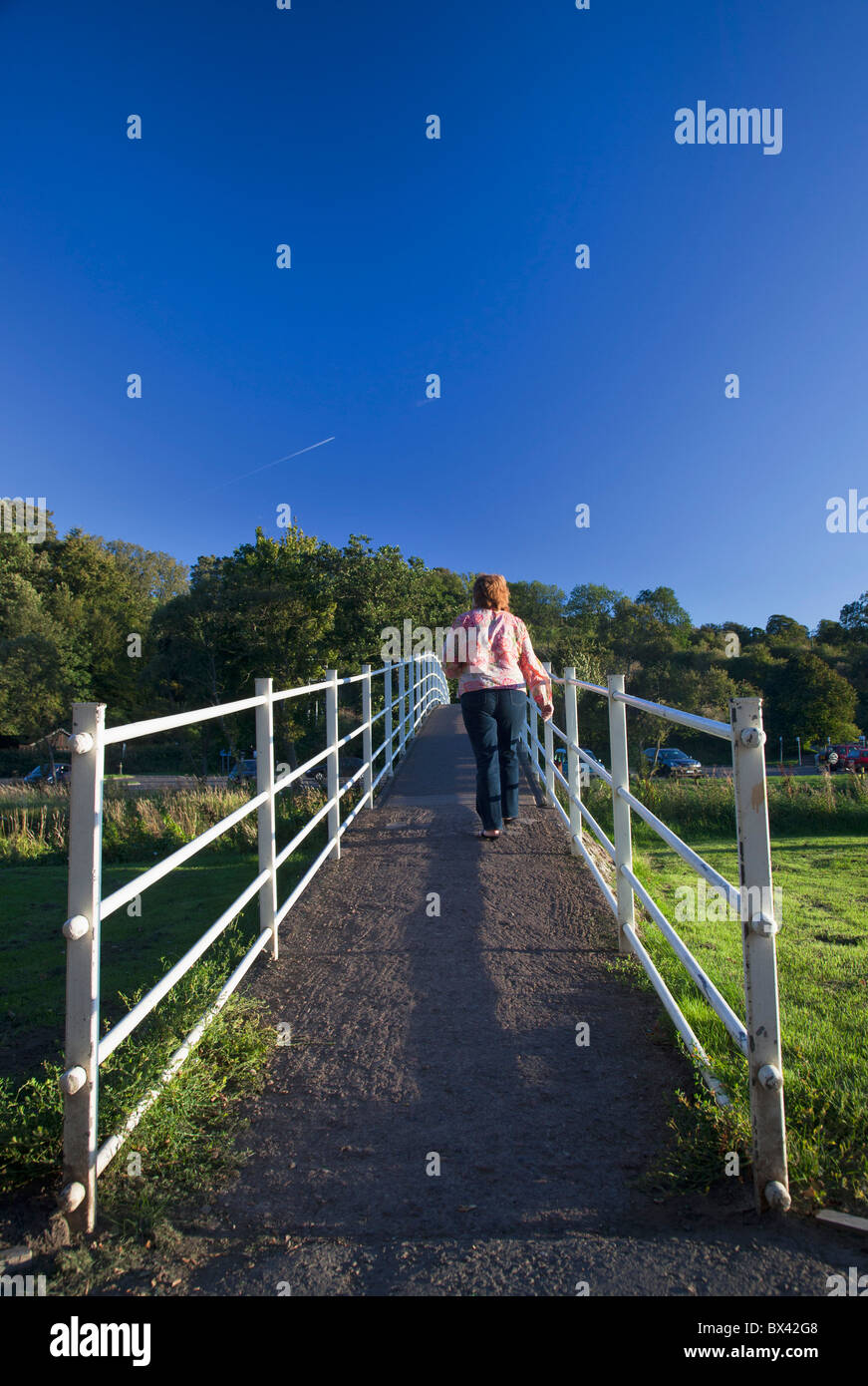 A Woman Walking Across A Footbridge; Rothbury, Northumberland, England ...