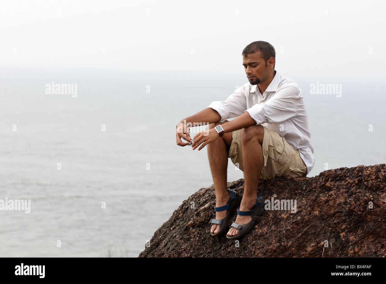 Young Indian male adult sitting on a rock Stock Photo - Alamy