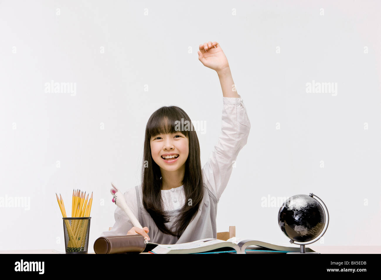 Girl with hand up, sitting at desk Stock Photo - Alamy