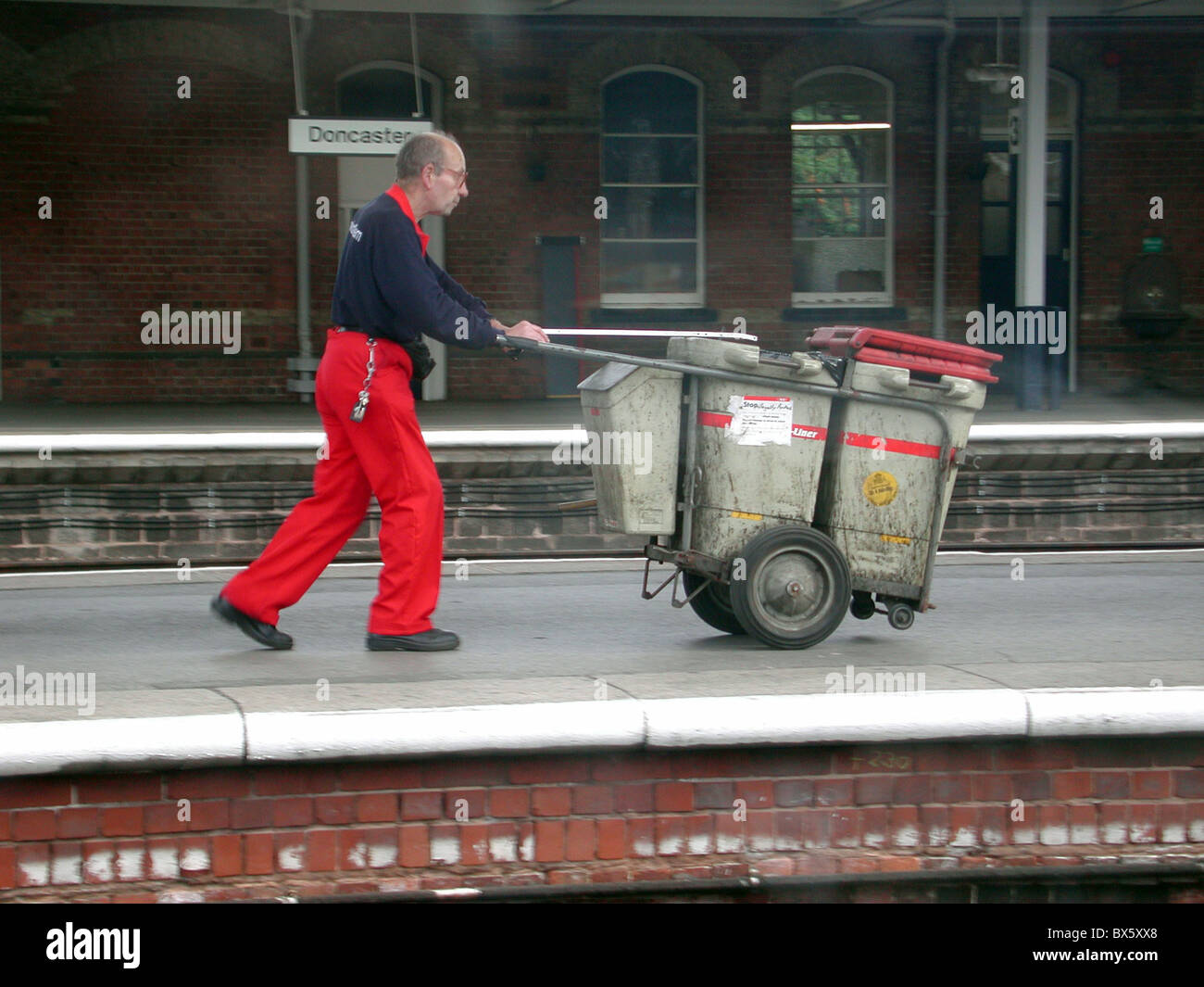 Dustman on train platform pushing bins on wheels Stock Photo - Alamy