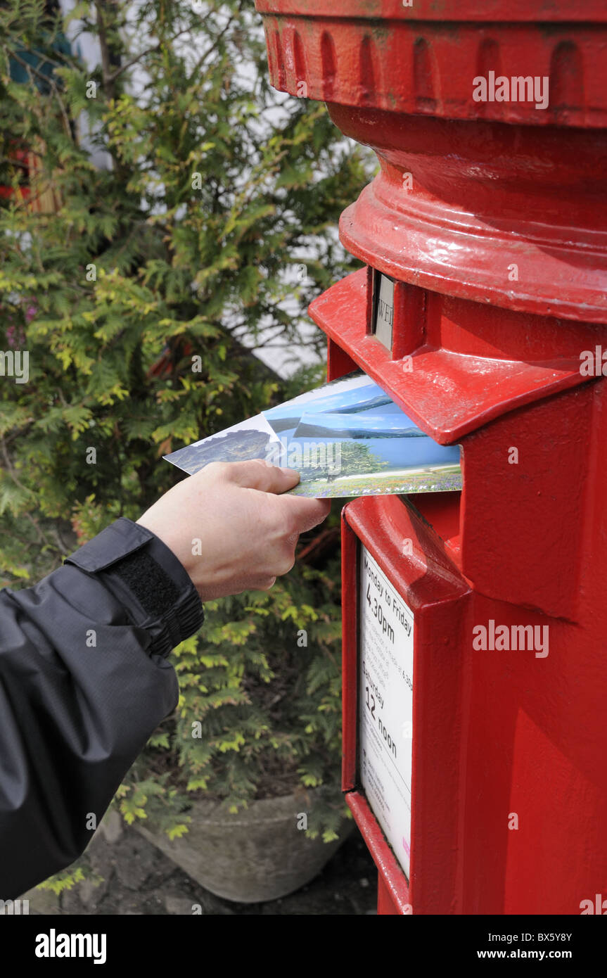 Posting postcards into a traditional red letter box Stock Photo - Alamy