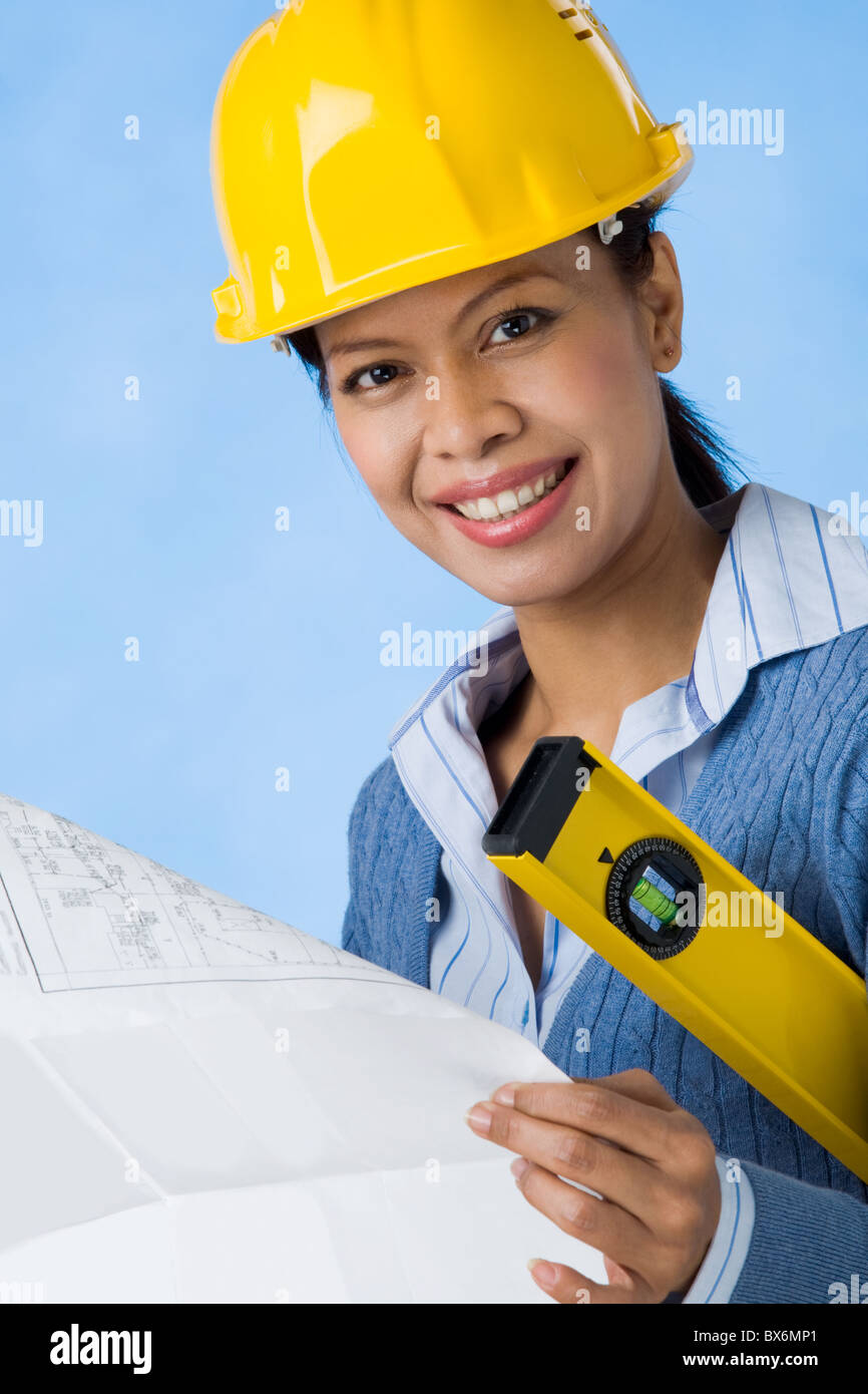 Portrait of pretty female with blueprints in hands and helmet on head ...