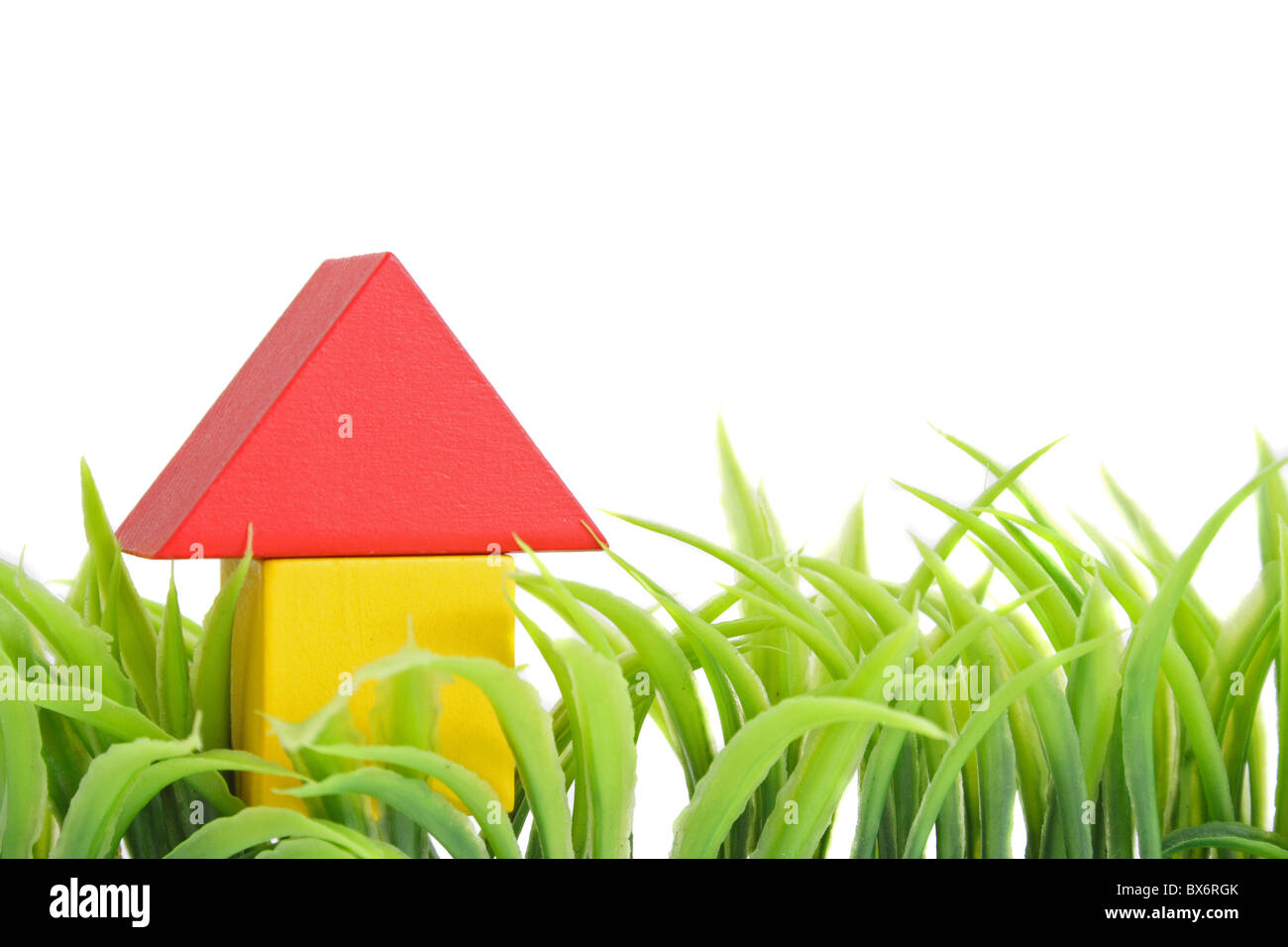 A stylized house out of colorful blocks between blades of grass. All ...