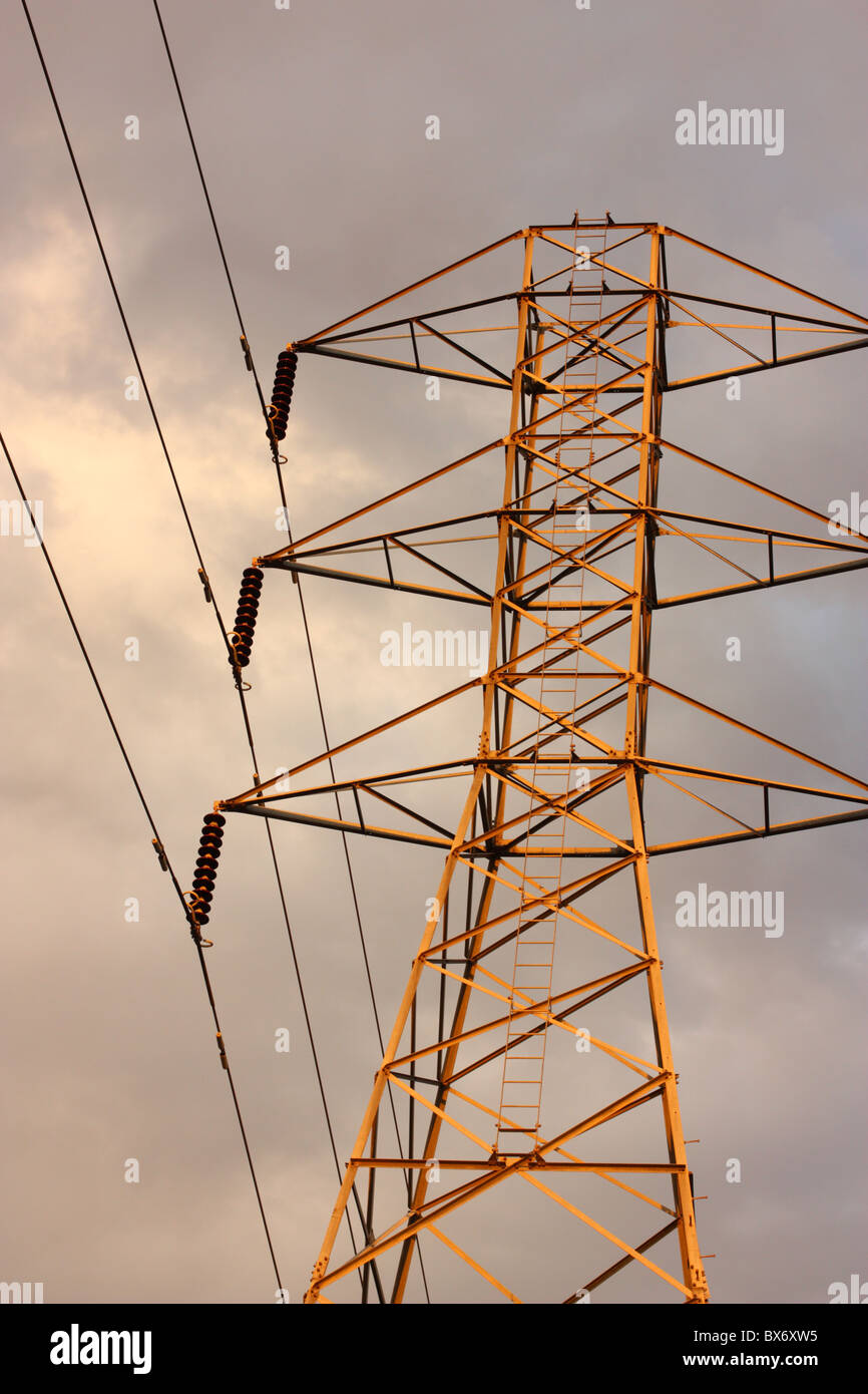 Transmission tower and power lines with bright sunset light shining on ...