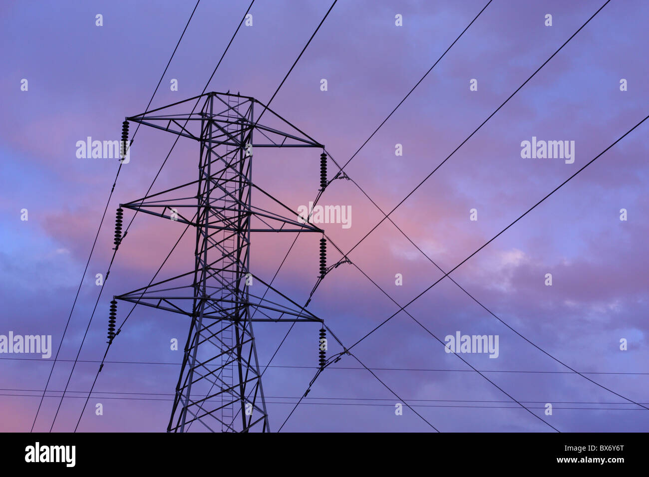 A transmission tower and power lines under a dramatic sunset sky ...