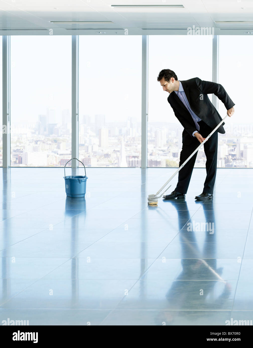 Businessman cleaning the floor in empty office, city landscape in ...