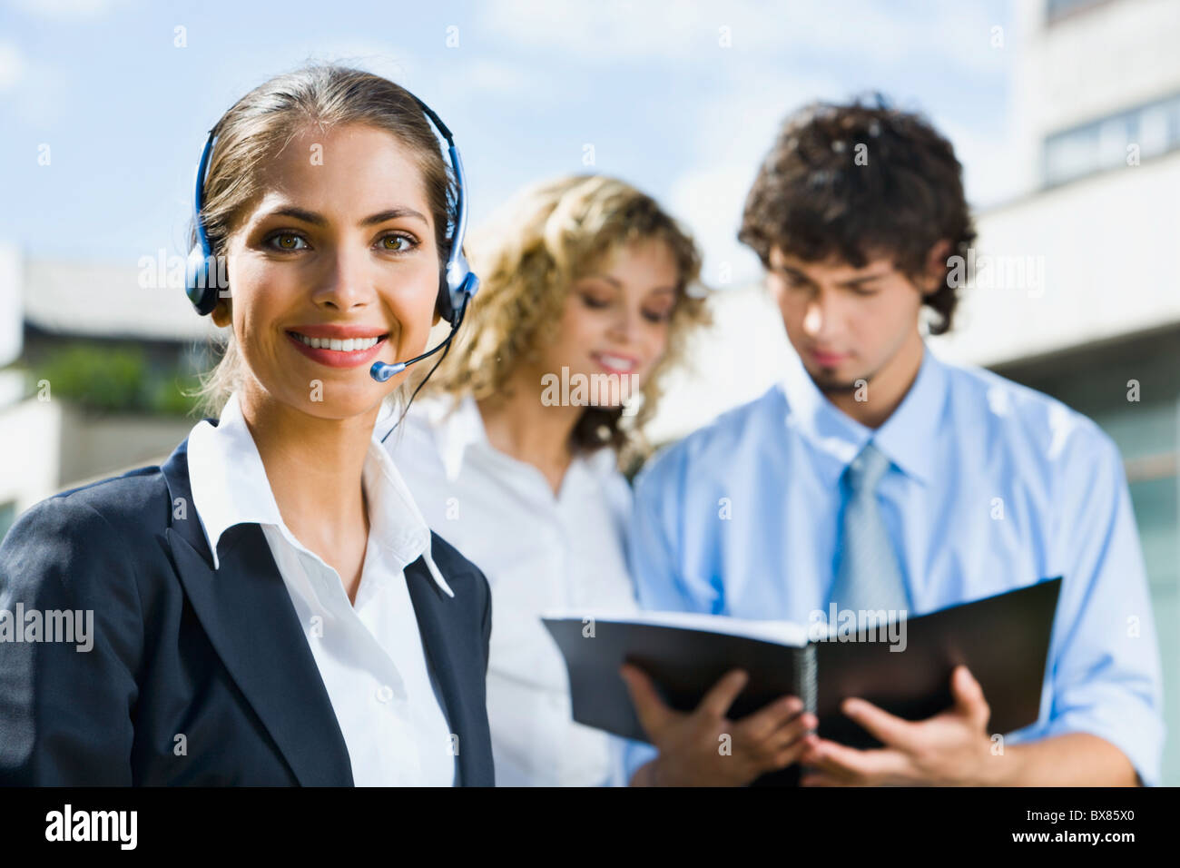 Portrait of smiling woman with headset on her head and two reading ...