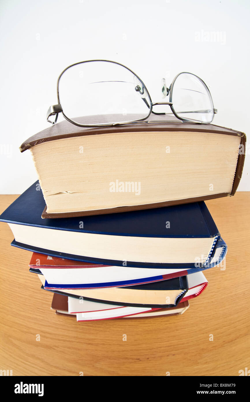 stack of open hardcover books and bifocal reading glasses on wooden ...