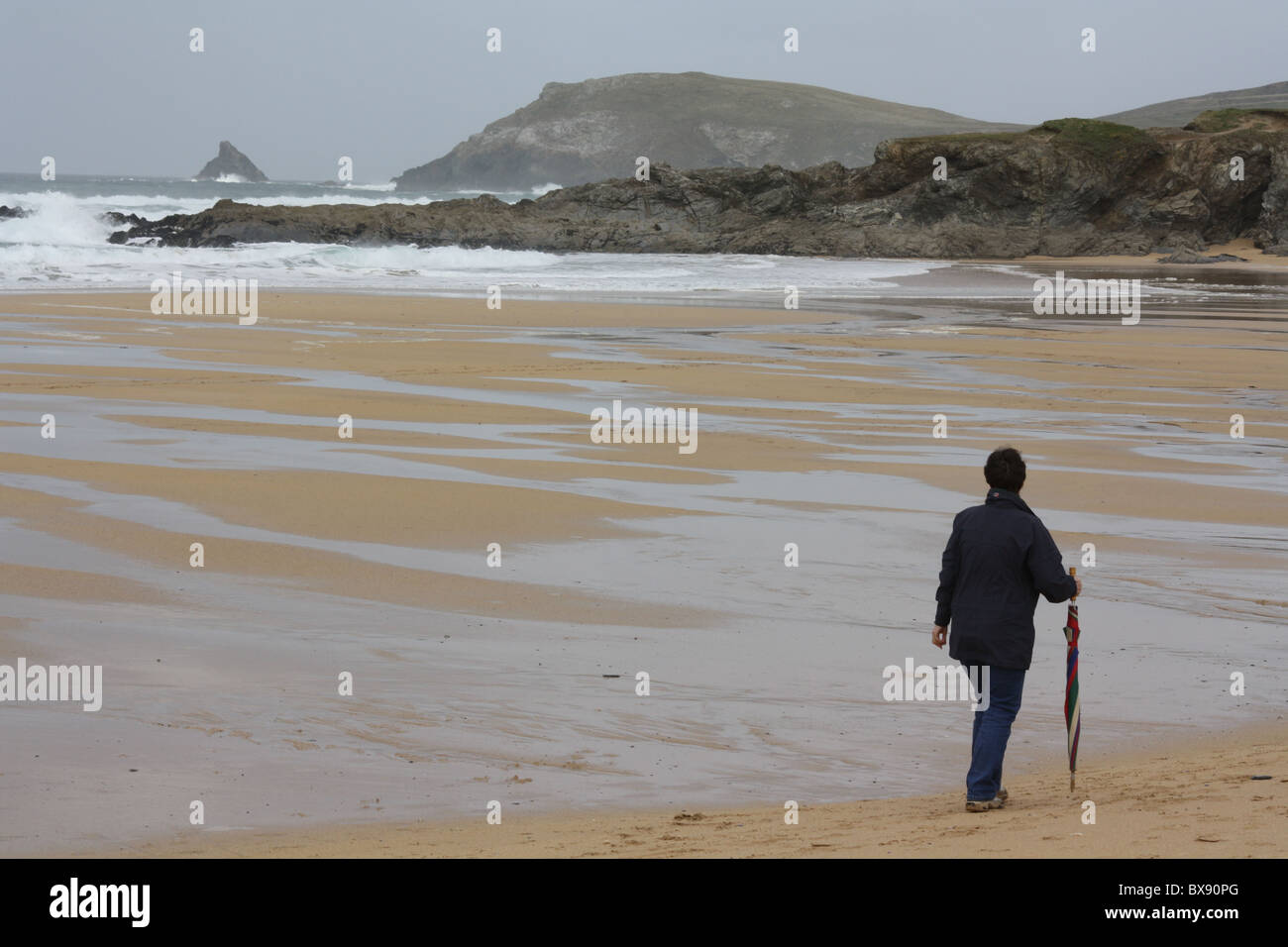 Lady using a long furled umbrella as a walking stick walks across a wet ...
