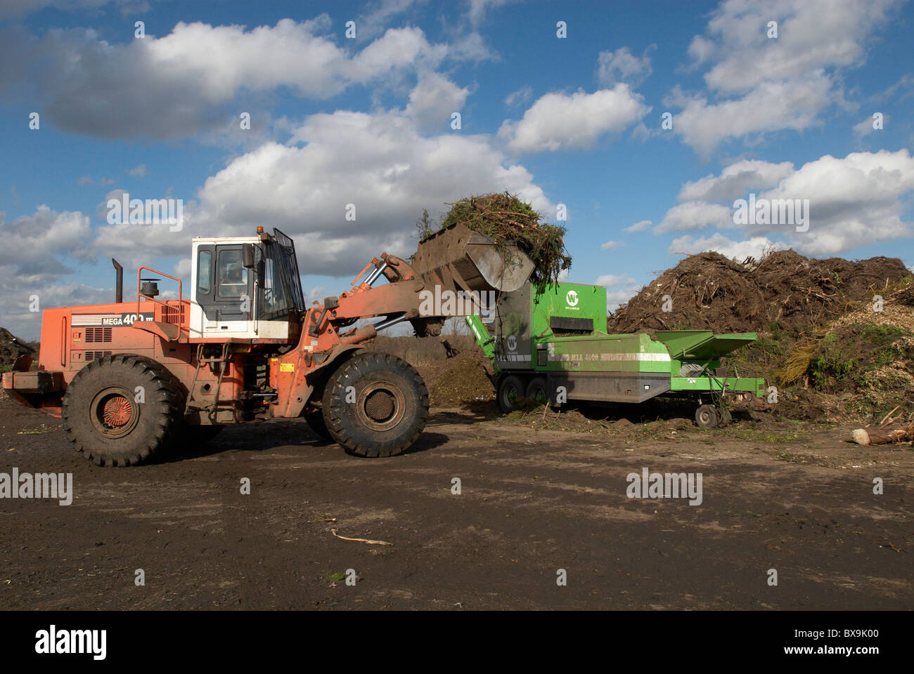 Front loader emptying garden waste into composting plant at site for ...