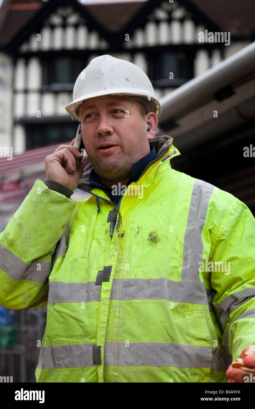 A man dressed in 'hi-viz' jacket and hard hat, makes a call on his ...