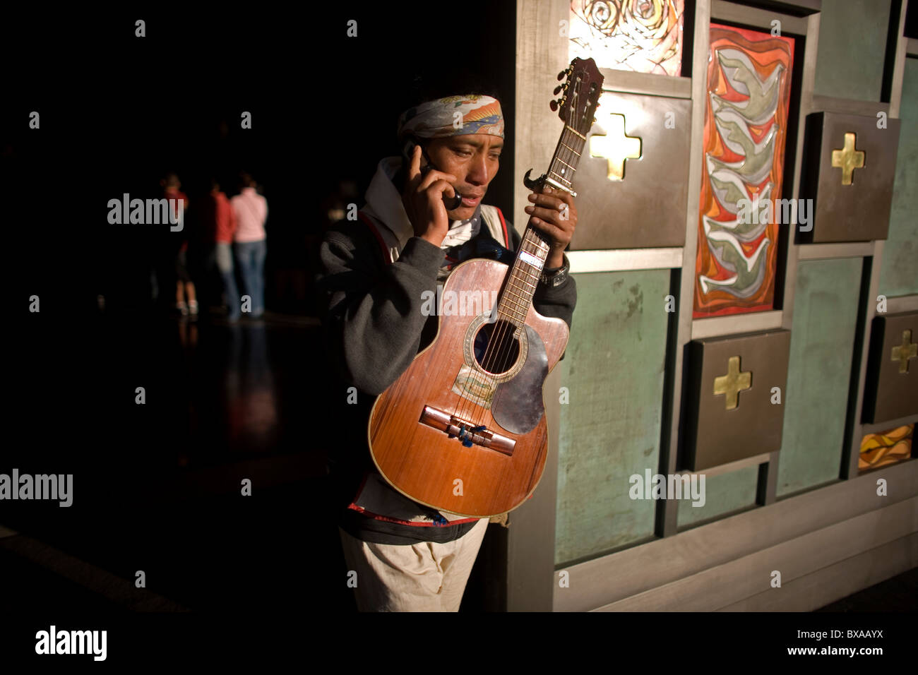 A pilgrim carries a guitar as he speaks by cell phone outside of the ...
