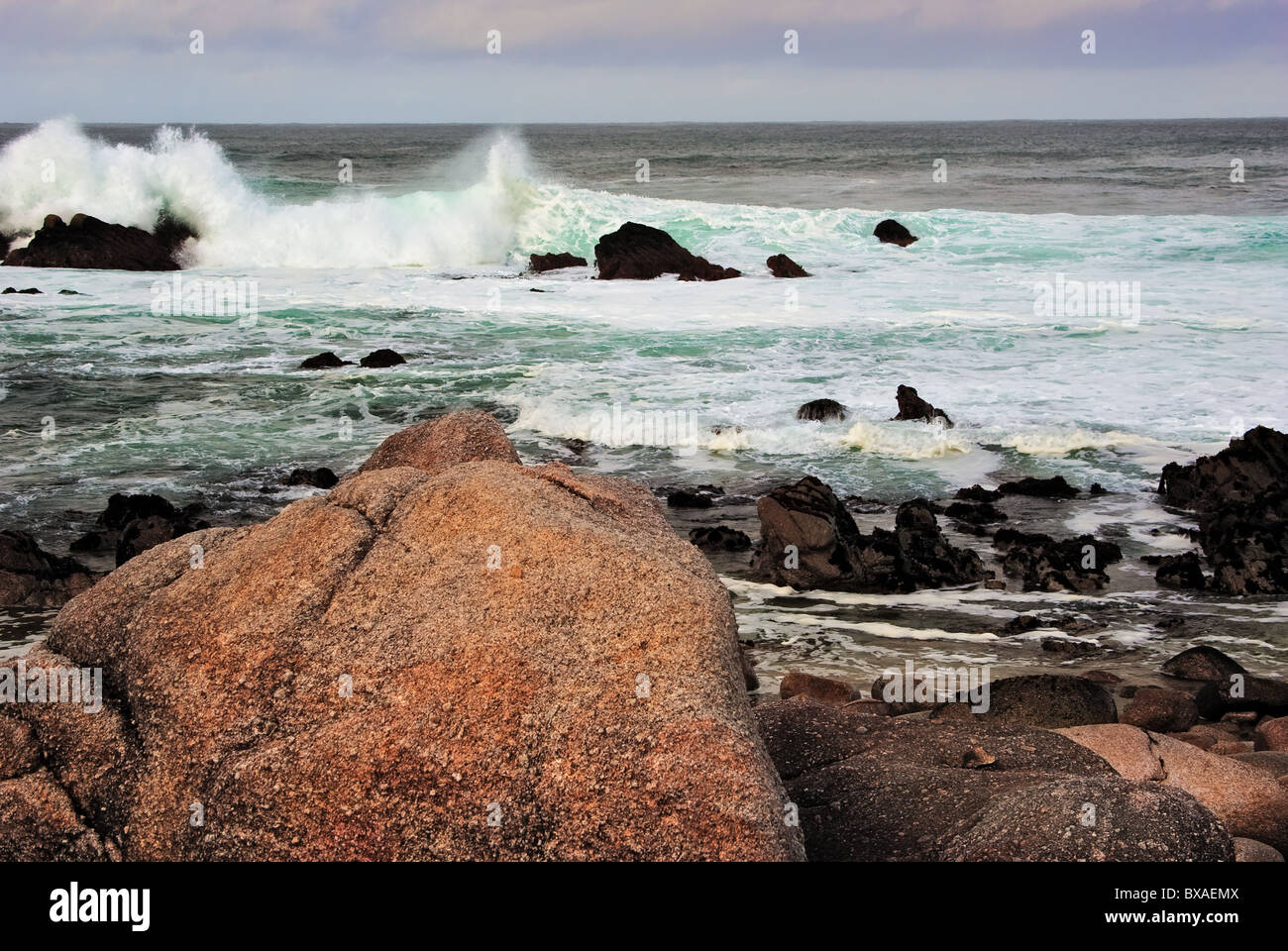 A colorful boulder sits in the foreground with large waves crash in the ...