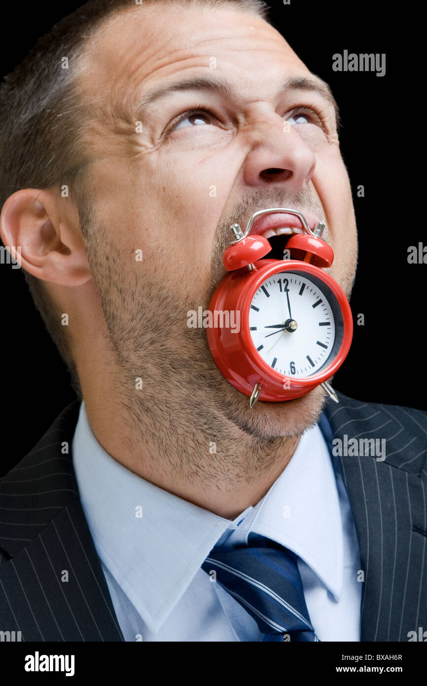 Man with a red alarm clock in his mouth; deadline or stress concept ...