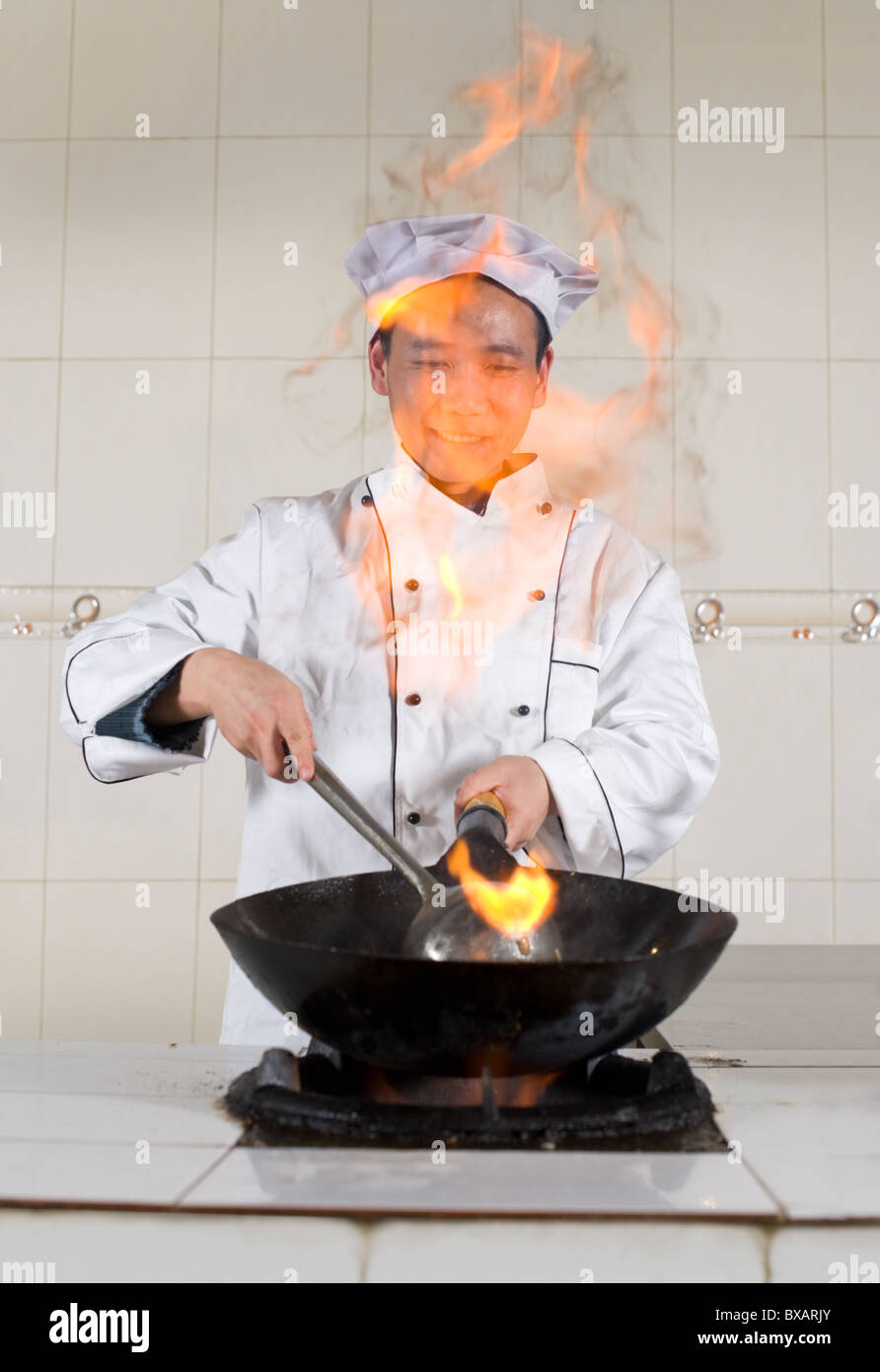 asian male cook at work in restaurant kitchen, fire flames over pan ...