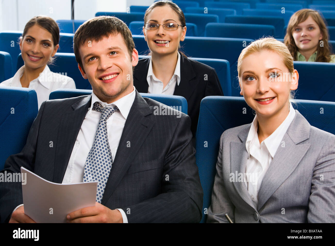 Group of smiling students sitting on the blue chairs in conference hall ...