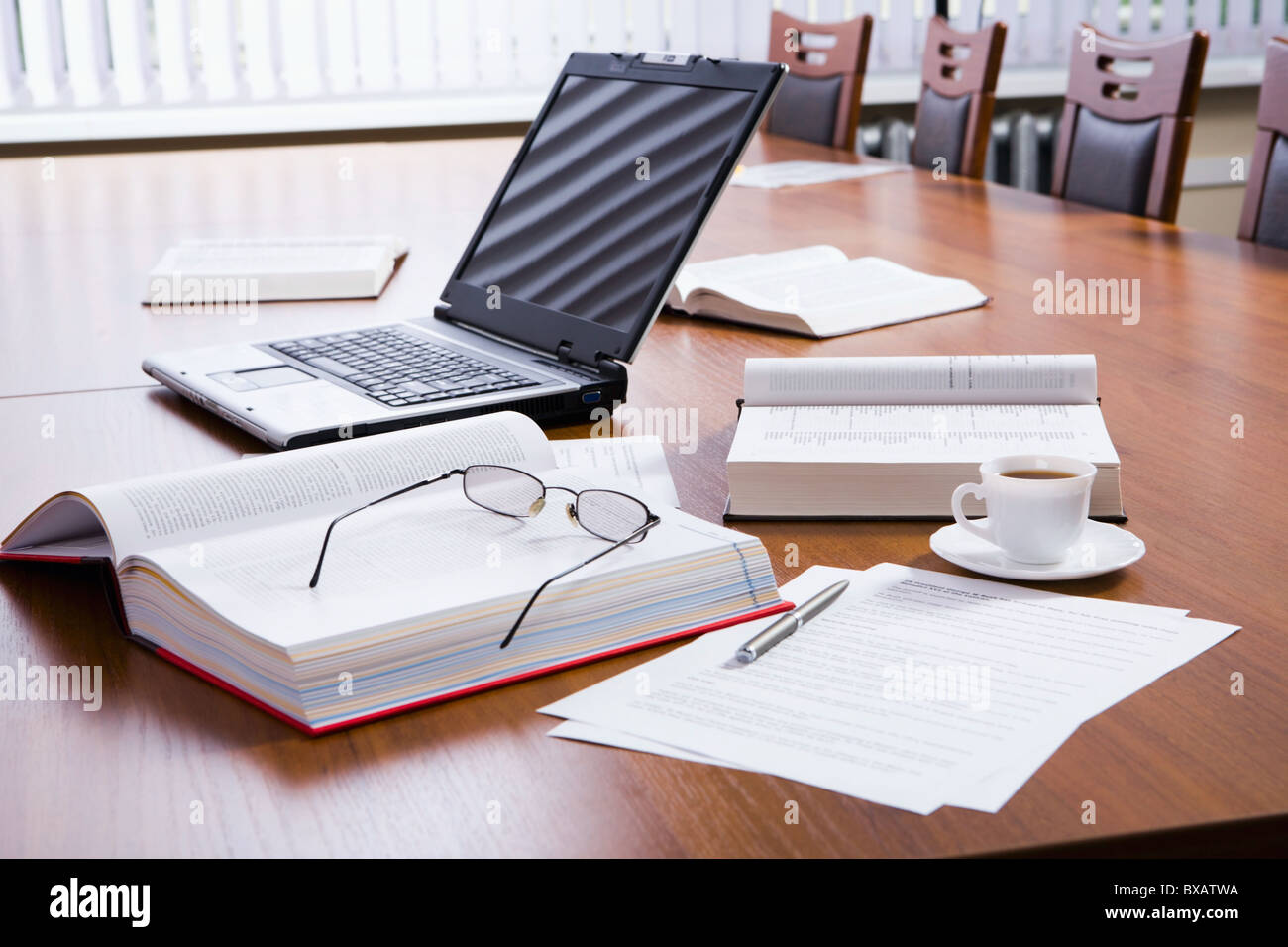 Opened thick books and laptop, documents, eyeglasses, pen and cup of ...