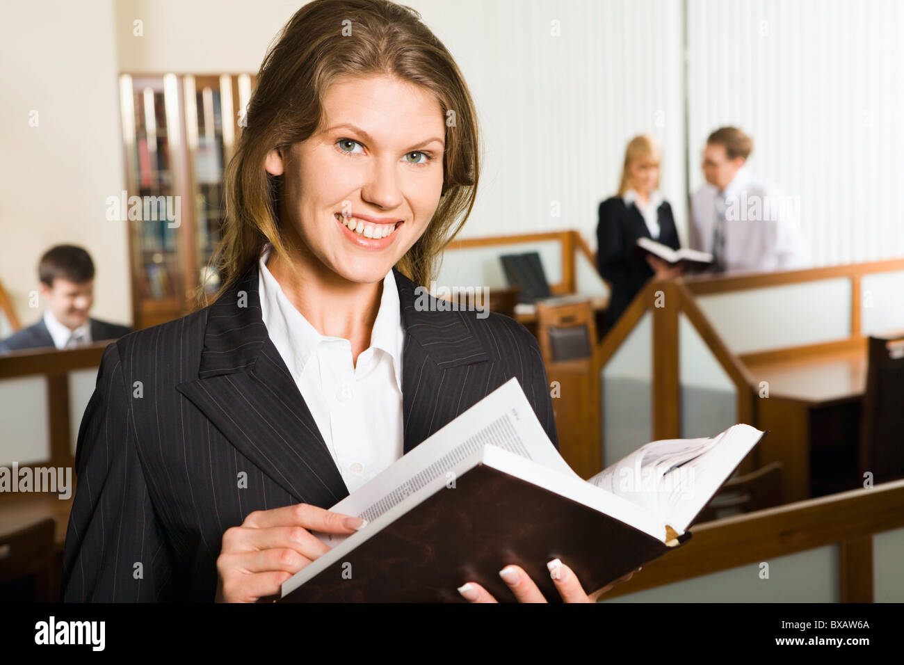 Portrait of smiling young student holding thick opened book gazing at ...