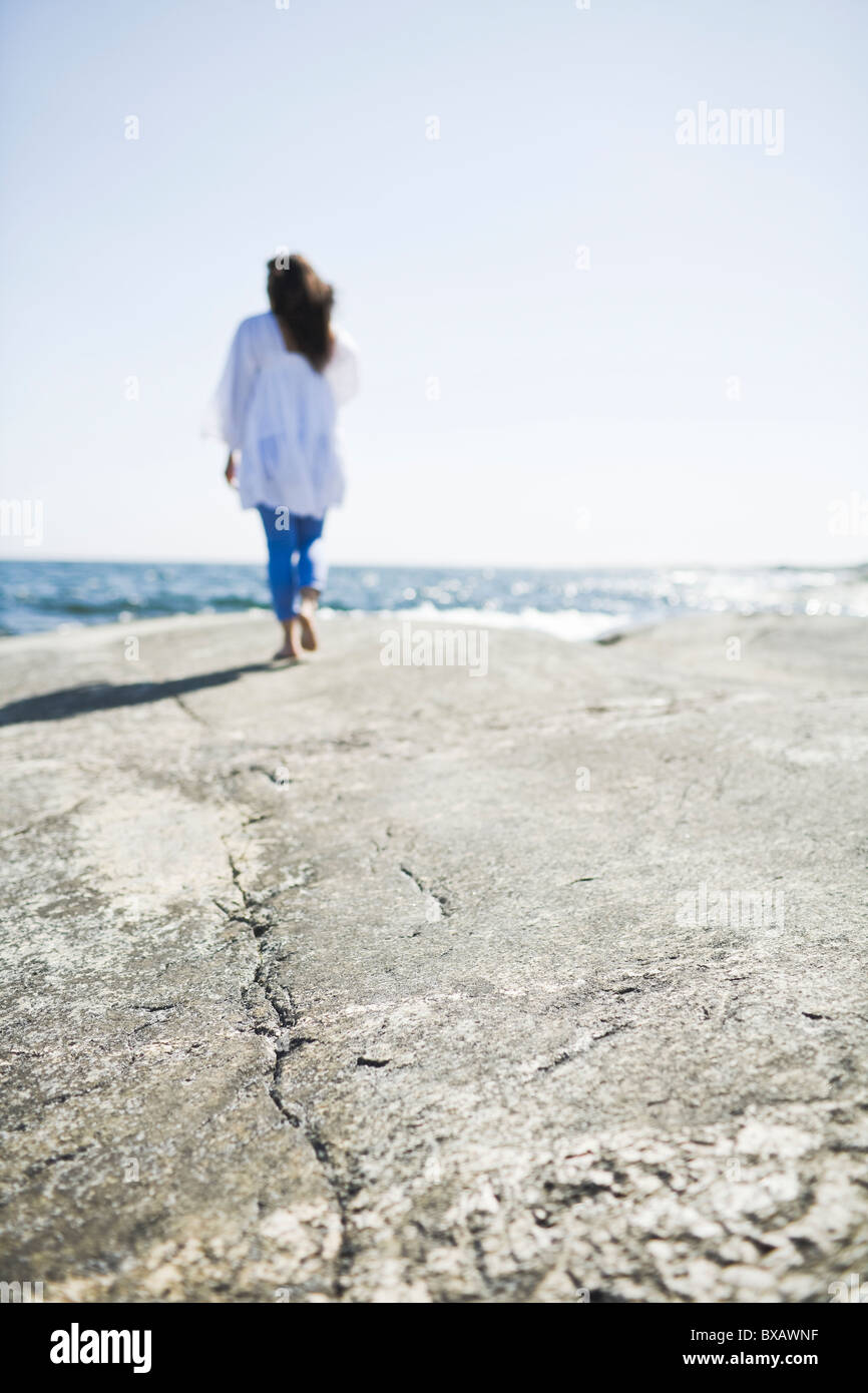 Woman walking on rock by sea Stock Photo - Alamy
