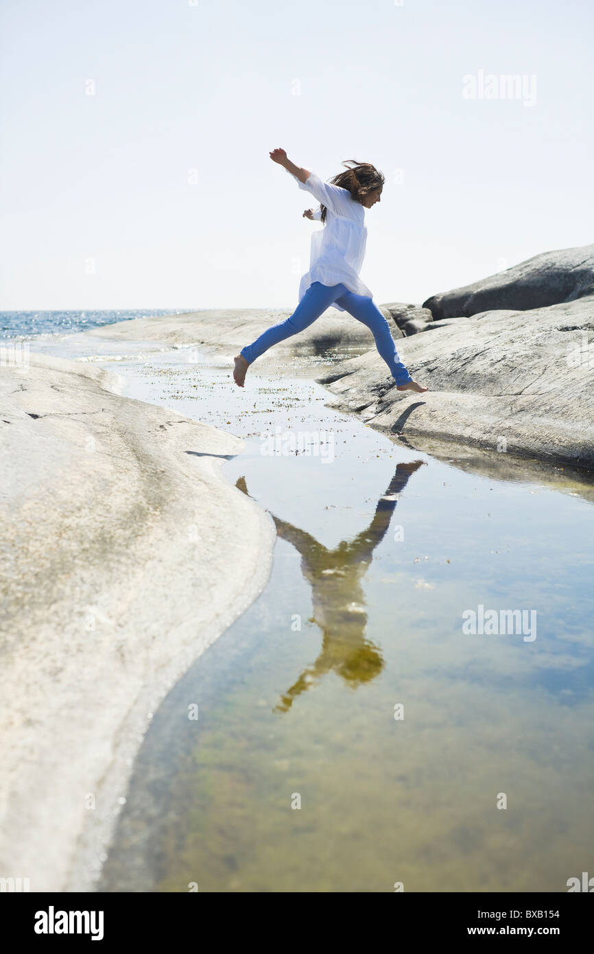 Woman jumping over water to rock Stock Photo - Alamy
