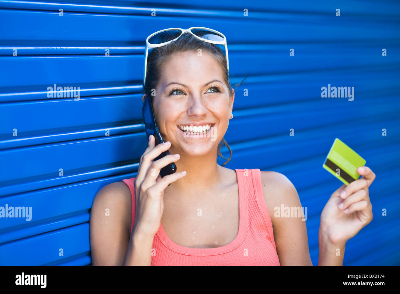 Young woman in front of blue wall, holding credit card and talking on ...