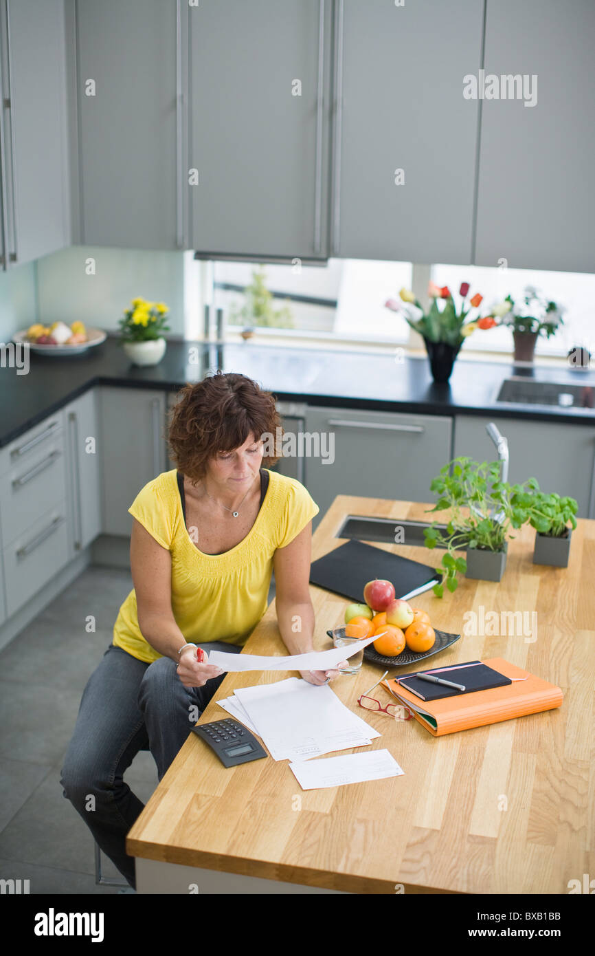 Woman sitting in kitchen with bills Stock Photo - Alamy