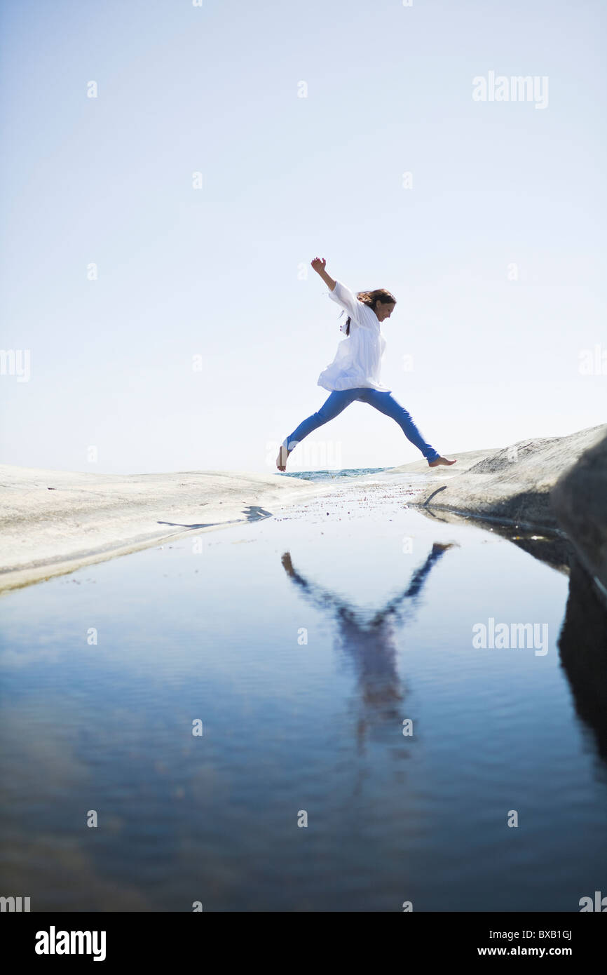 Woman jumping over water to rock Stock Photo - Alamy