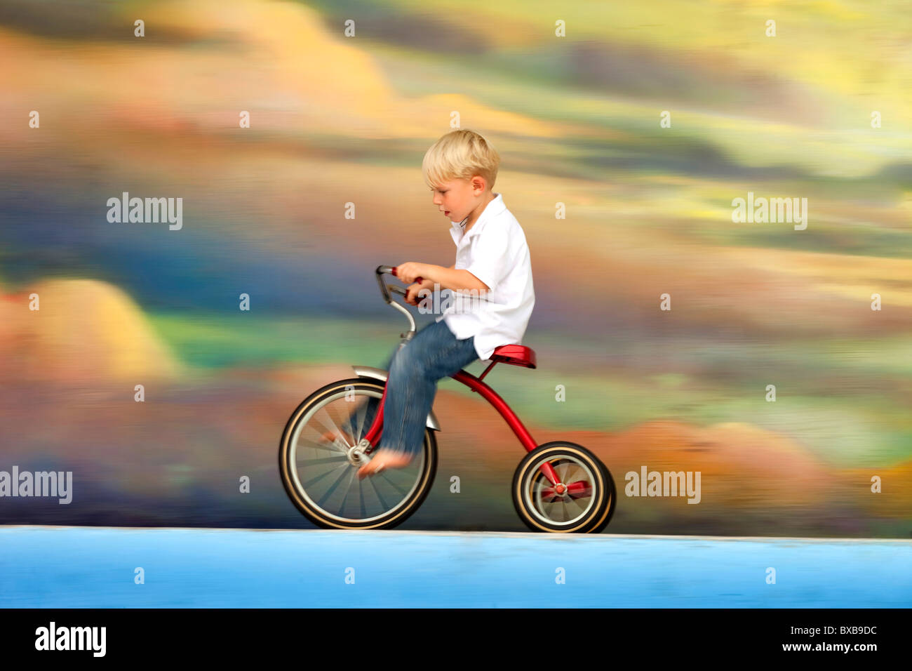 Young boy riding tricycle against colorful sky with clouds Stock Photo ...
