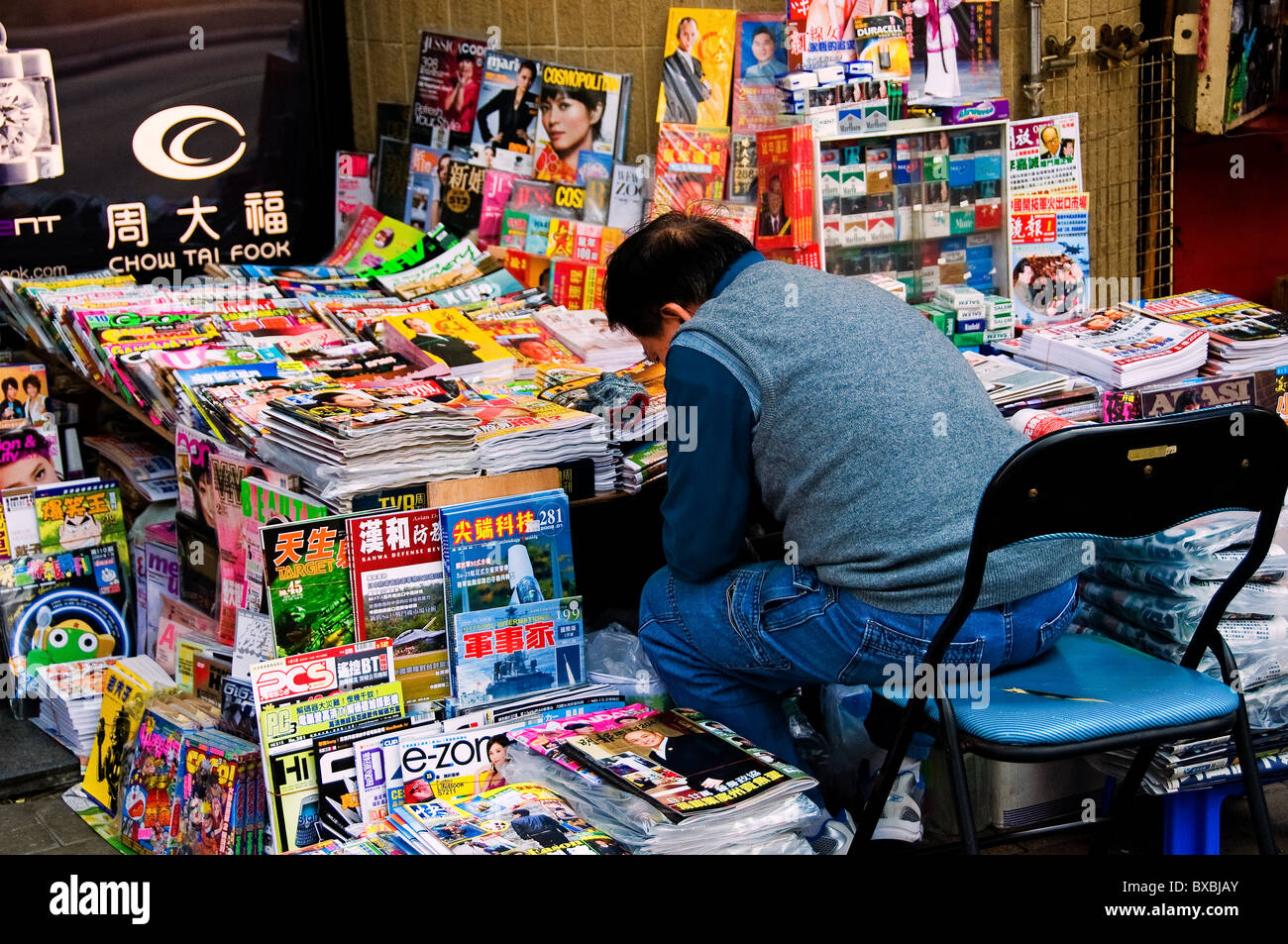 Asian man sitting at newsstand on city street in downtown Hong Kong ...