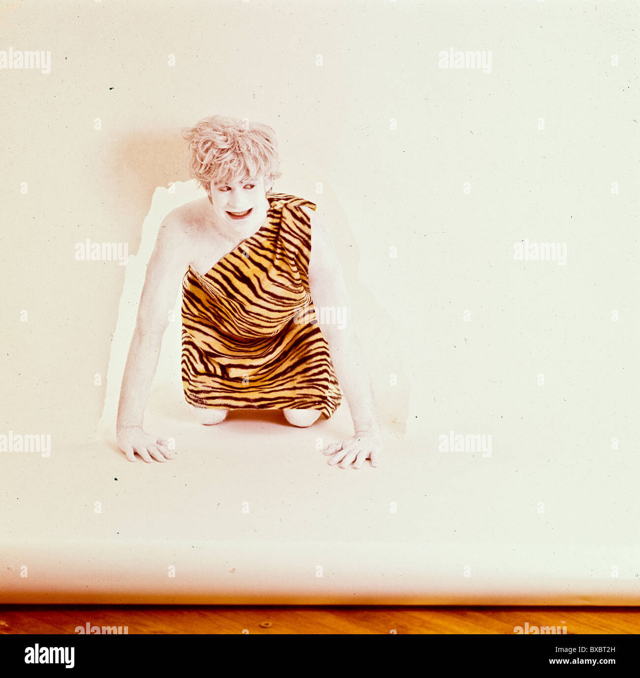 White face, faced male mime tiger skin caveman crawls from paper cave ...