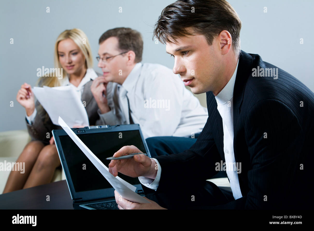 Portrait of serious man reading a document with open laptop and two ...