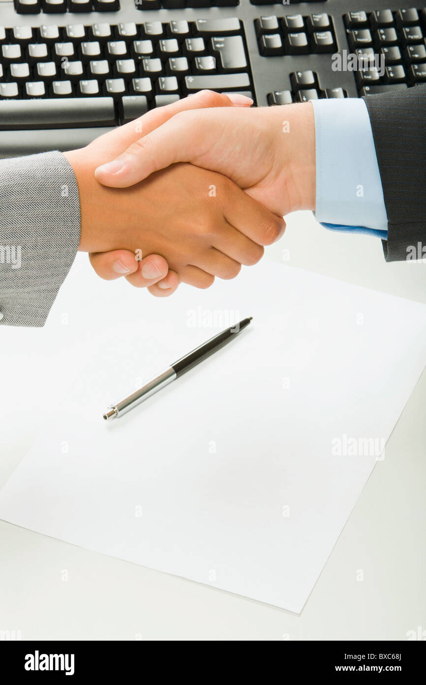 Woman and man shaking hands over blank paper and pen, keyboard on the ...
