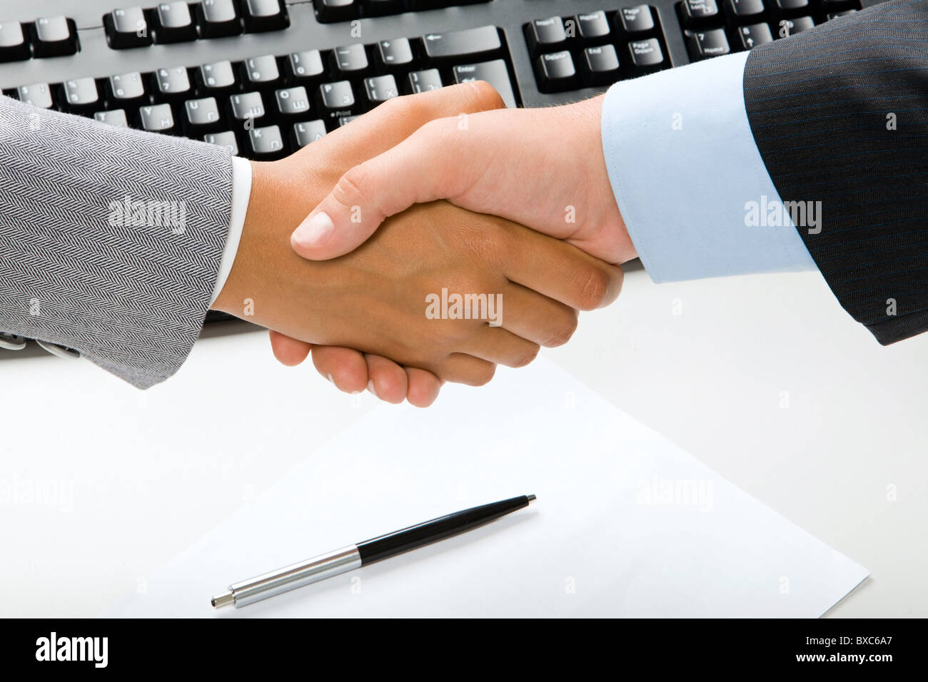 Woman and man shaking hands over blank paper and pen, keyboard on the ...