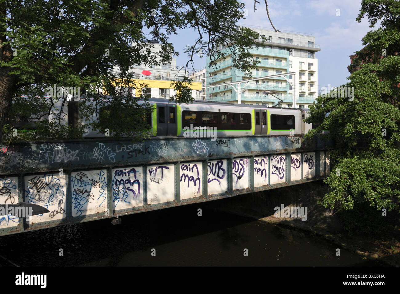 Commuter train on canal side rail bridge adorned with graffiti at ...
