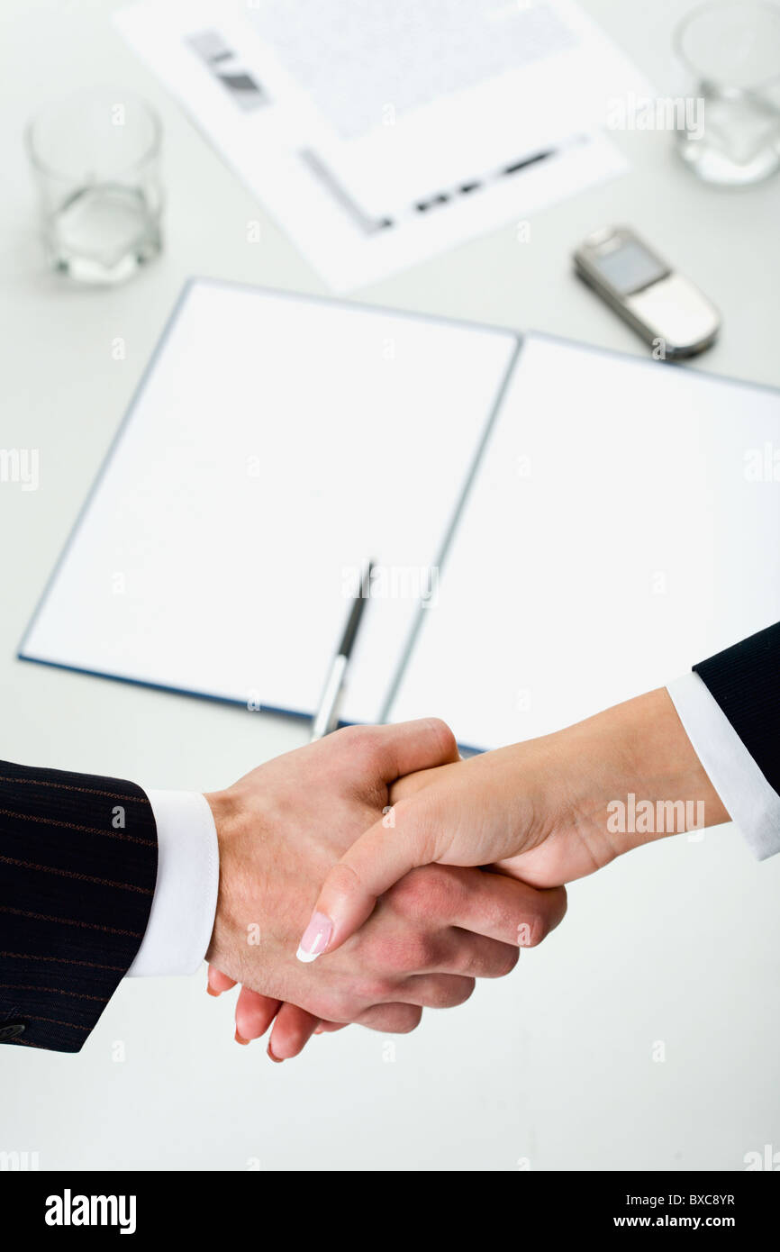 Woman and man shaking hands over paper, pen, phone, glasses on the ...