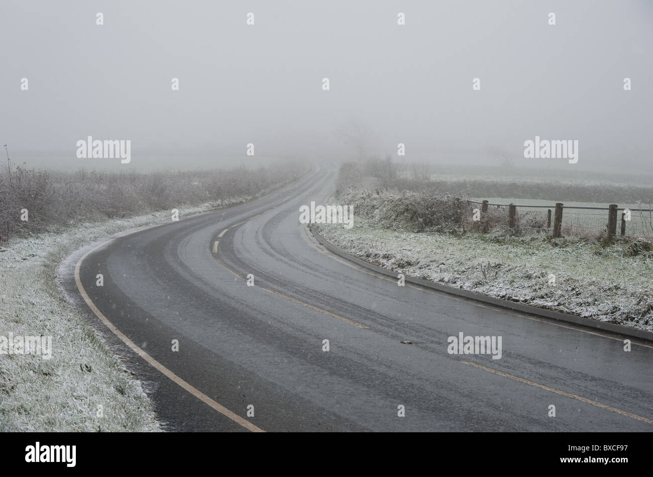 Rural winter scene, overcast, snow falling lightly, empty road with ...