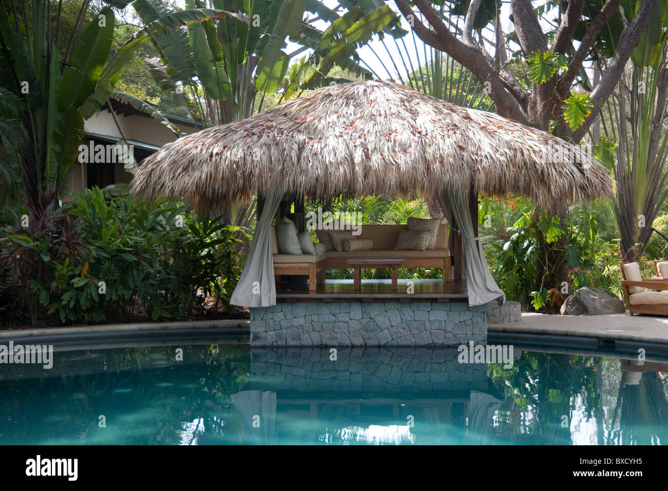 Open sided poolside cabana with palm leaf roof and sofa lounge Stock ...