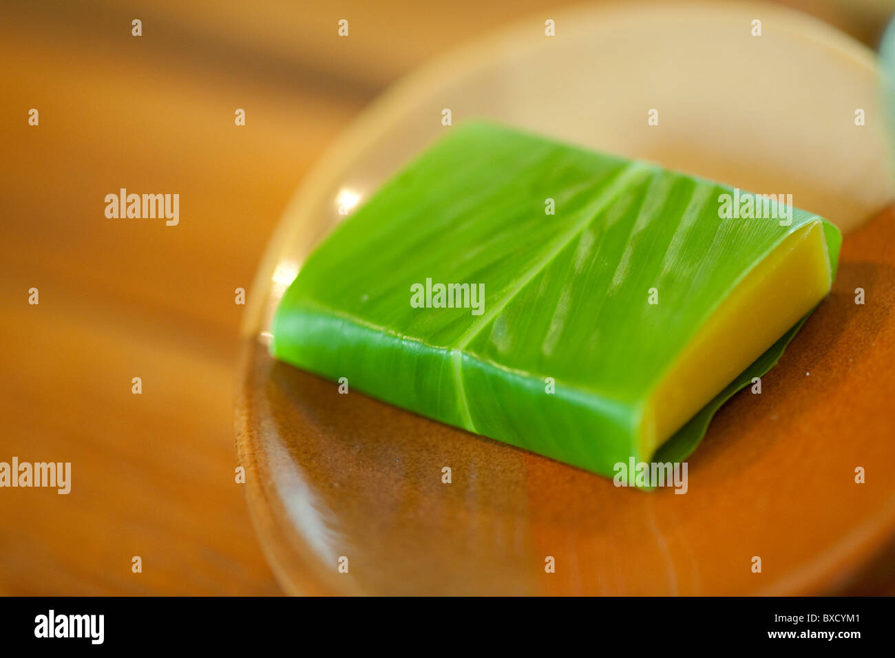 Yellow bar of soap wrapped in a green leaf sitting in a wooden soap ...