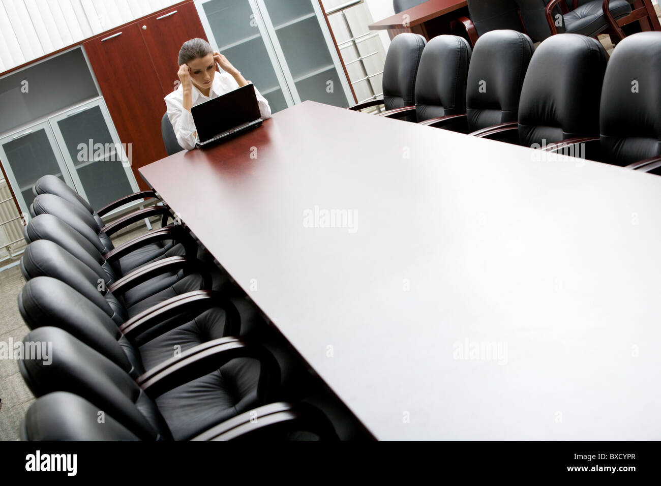 Business woman sitting at a large wood table with laptop on it and ...