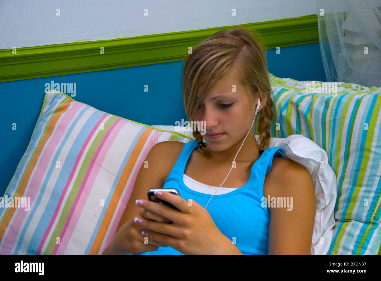 Teen girl texting with headphones in ear, has a French manicure and ...