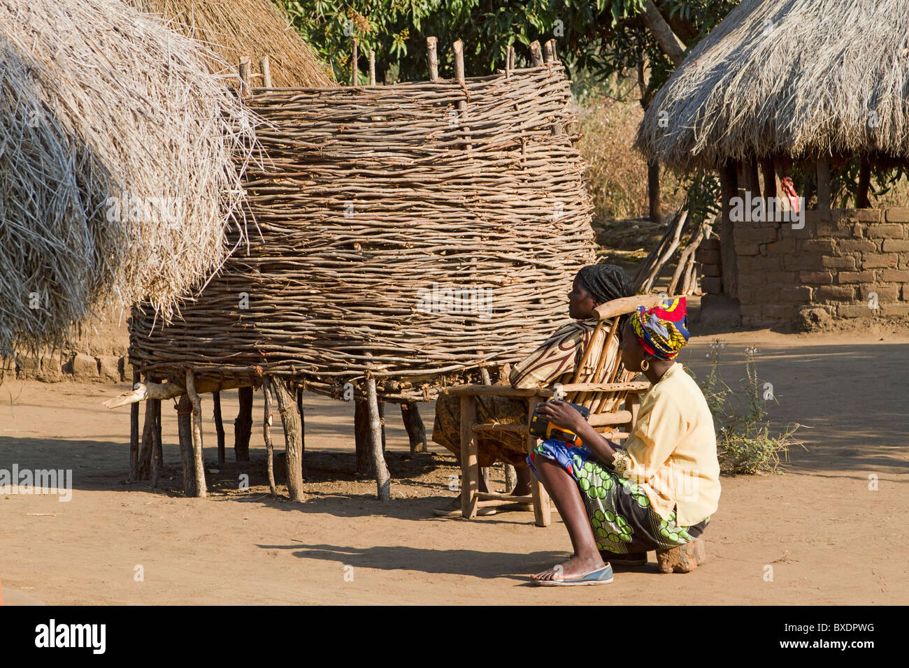 Young women, 20s, sit outside their thatch hut in their village, Kawaza ...