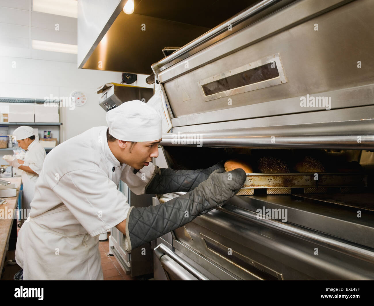 mid adult female chef putting baking-pan into oven Stock Photo - Alamy