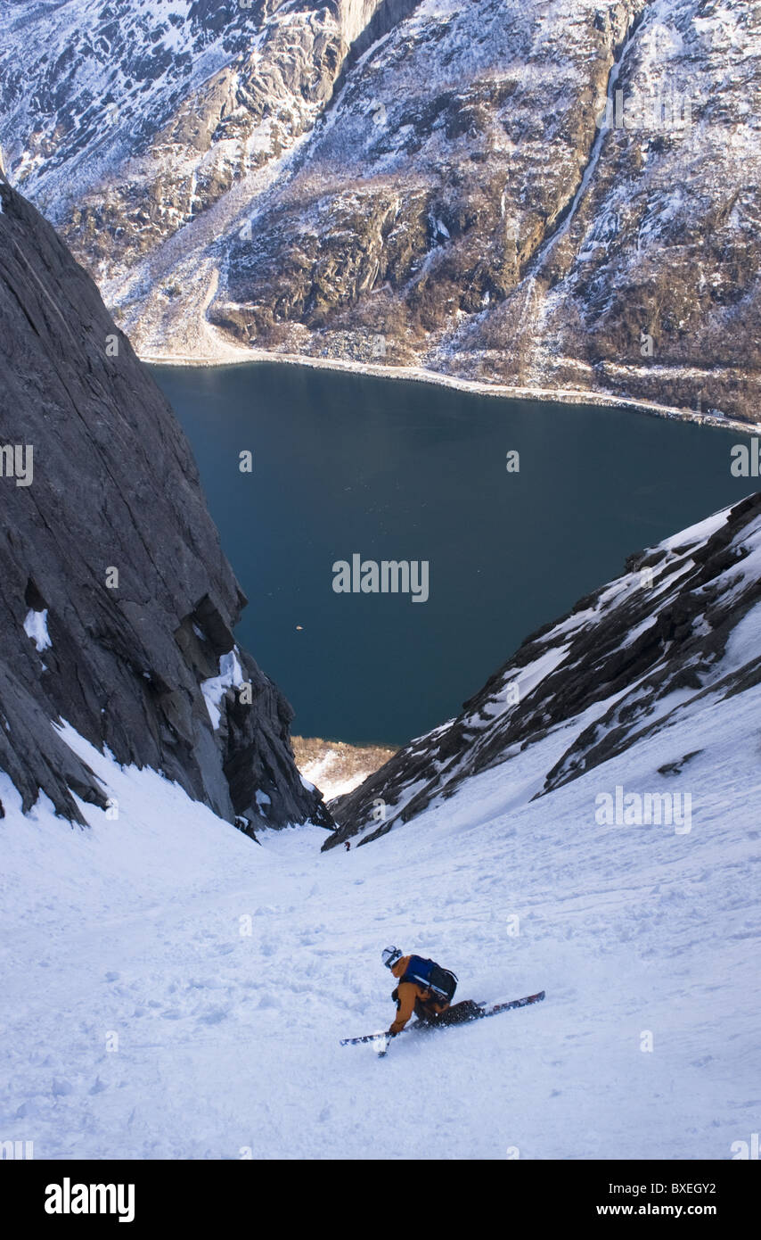 A male telemark skier skiing down a steep, rock-walled couloir in ...