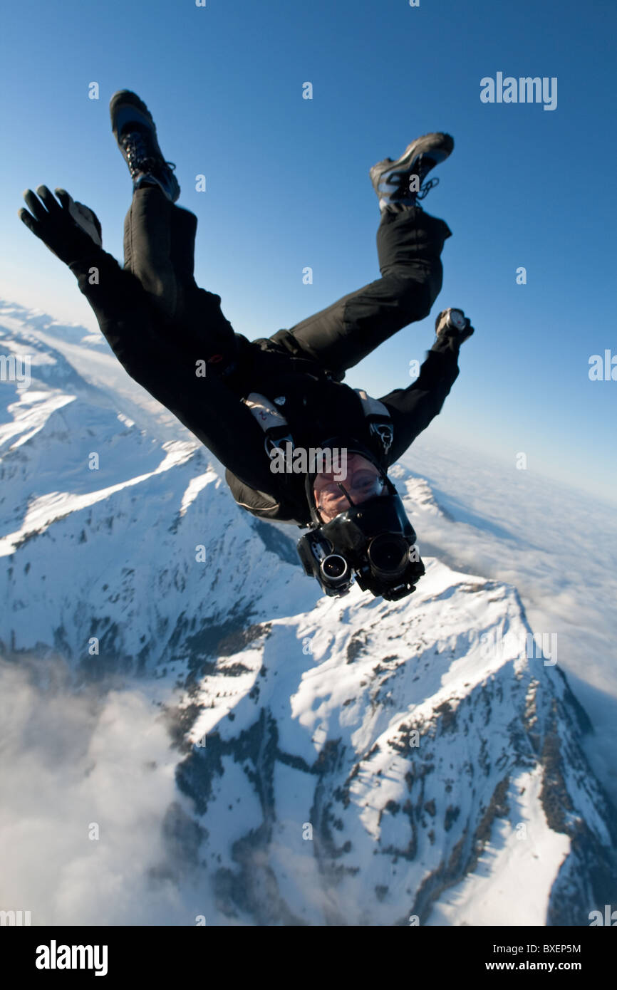 Man with camera on his helmet is filming skydiver in freefall over snow ...