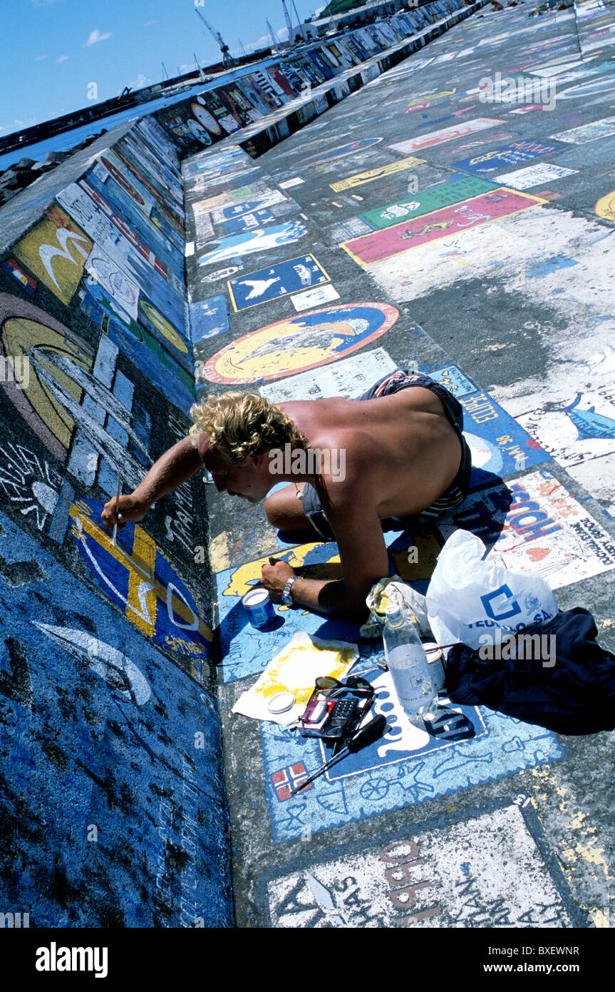 A visiting yachtsman hand-paints a ship's calling card on the marina ...