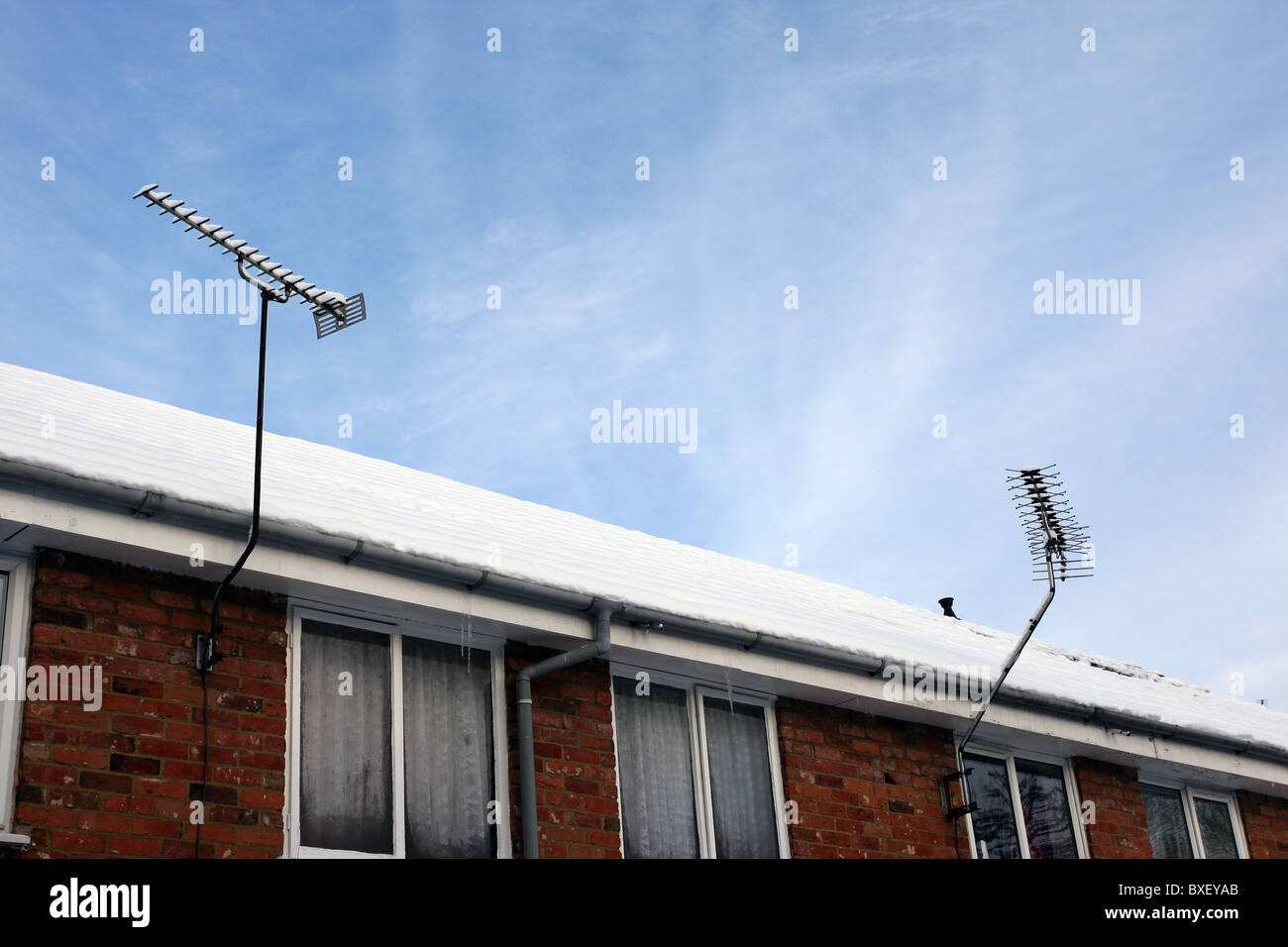 Rooftops and television aerials under snow against a blue sky in winter ...