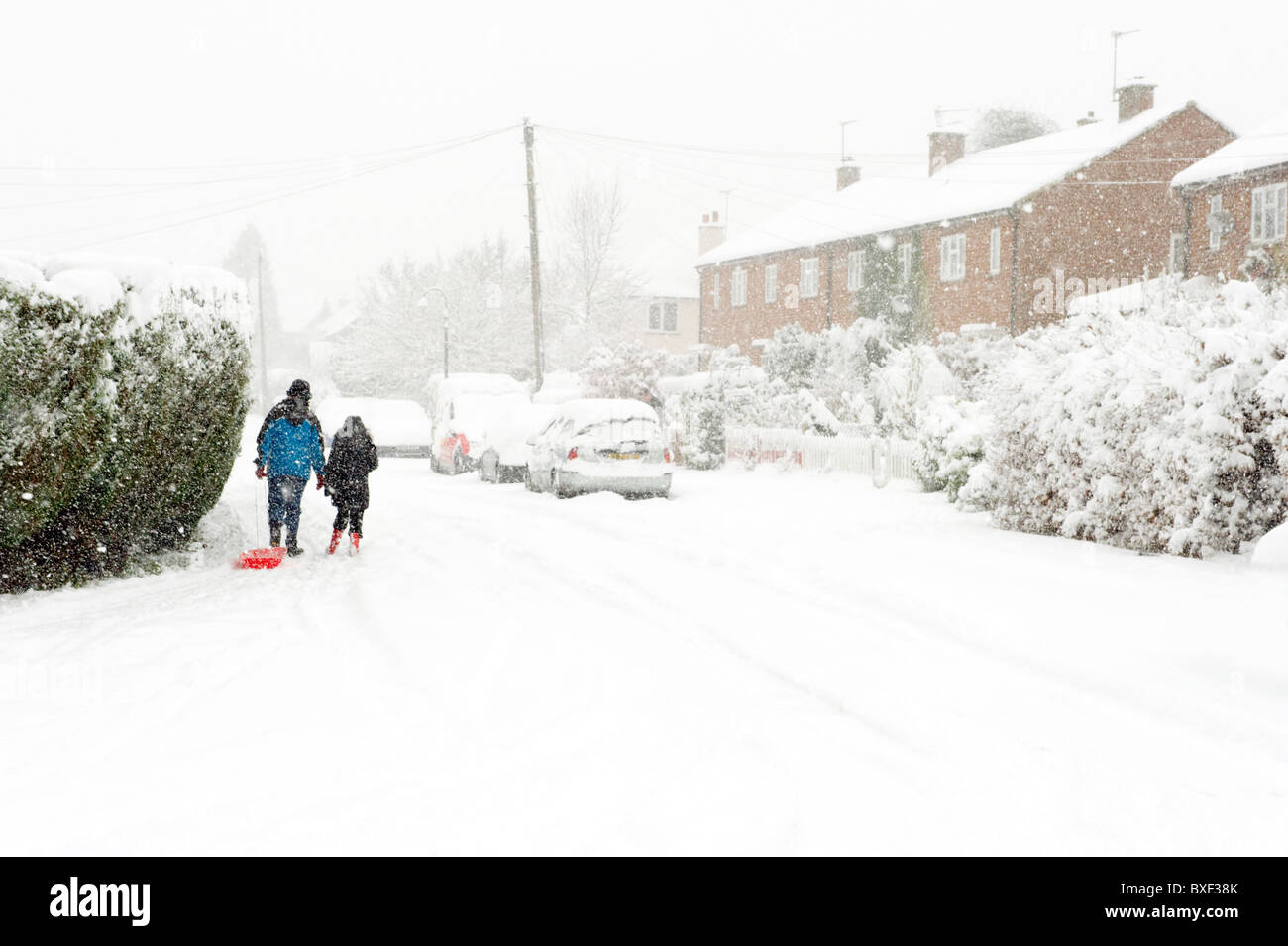 man and child with red toboggan walk along a snow covered road in a ...